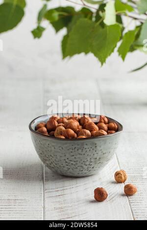 A handful of hazelnuts in a grey bowl on a white wooden background ...
