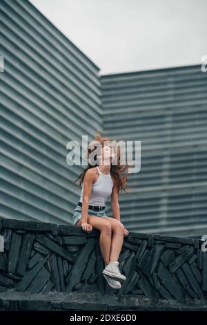 Young urban woman sitting against a white wall Stock Photo - Alamy