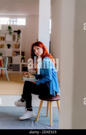 young redhead freelancer sitting on concrete bench and using laptop ...