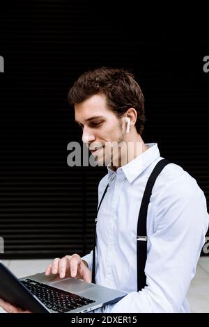 Contented businessman with laptop standing by building Stock Photo - Alamy