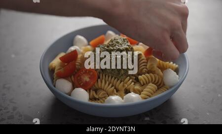 man add cherry tomatoes to pesto penne on black plate, wide photo Stock ...