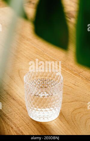 High angle of faceted glass with fresh water placed on wooden table ...