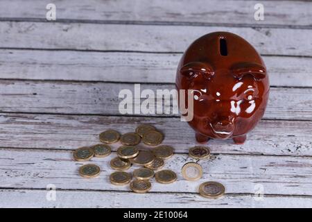 Brown glazed piggy bank and British coins. Focus on standing pound coin ...