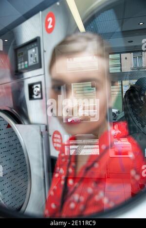Young blonde woman waiting for washing machine studying at laundry room ...
