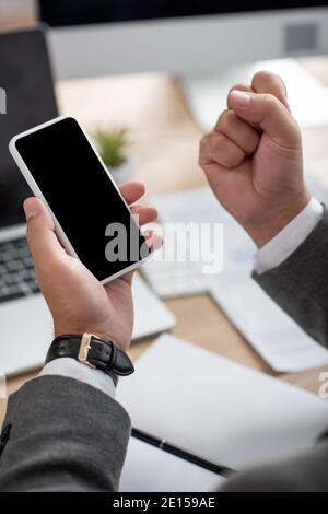 partial view of trader holding smartphone near laptop, computer ...