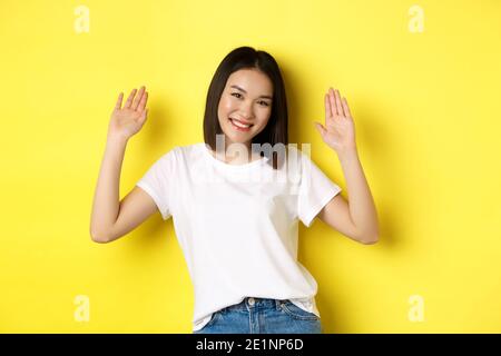 Friendly young asian woman saying hello, raising empty hands up and ...