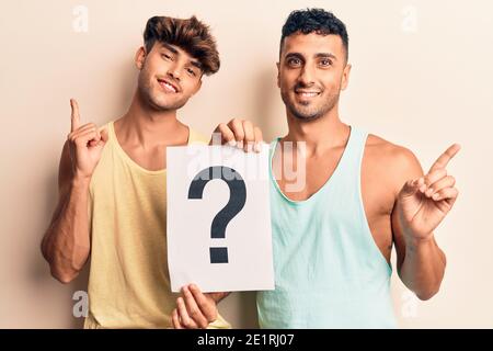 Young gay couple holding question mark smiling happy pointing with hand ...
