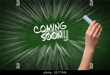 Hand drawing COMING SOON inscription with white chalk on blackboard ...