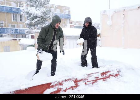 Two men removing snow from the roof of their house. Snowstorm, blizzard ...