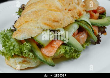 Croissant sandwich with red fish, avocado, fresh vegetables and arugula ...