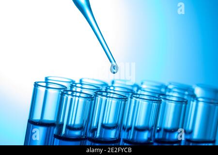 Closeup shot of a pipette tip with a droplet over glass test tubes ...