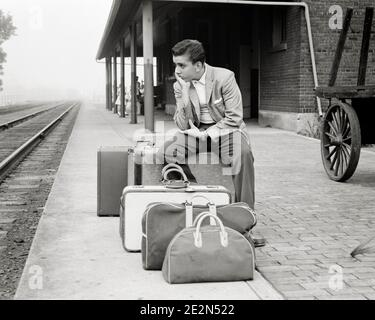 Depressed man sitting on the railroad tracks, holding phone, makes a ...