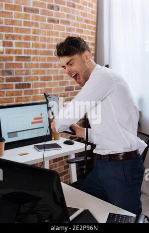 Mad businessman screaming while holding keyboard near computer on ...