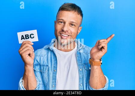 Handsome muscle man holding abc letters on paper smiling happy pointing ...