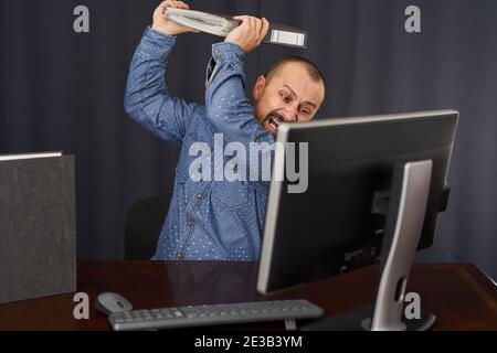 Angry businessman smashing computer screen with a folder of documents ...