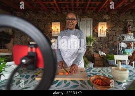 Happy Afro senior woman preparing food recipe while streaming online ...