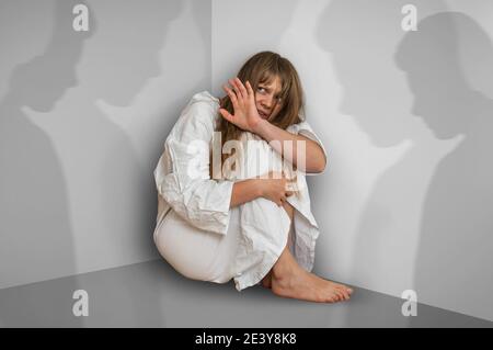 Scared woman with schizophrenia sitting in the corner at room with ...