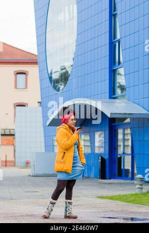Young female in coat recording voice message on smartphone standing ...