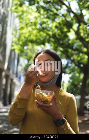 African american woman with lowered facemask with coffee cup using ...