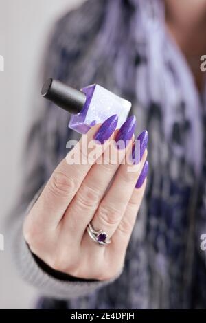 Female hand with long nails and purple lilac manicure holds a bottle of ...