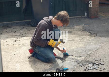 Builder chopping concrete with chisel and hammer wearing grey jacket ...