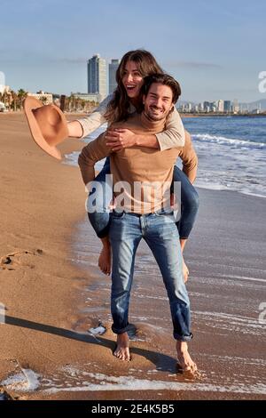 Smiling man piggybacking woman while standing by window at front yard ...