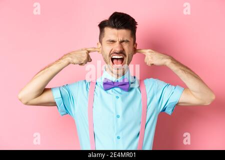 Irritated young man block noise, shut ears with hands and screaming ...