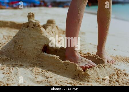 Isla Mujeres, Cancun, Mexico. Child's feet dance around the sand castle ...