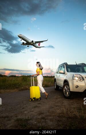 woman with luggage near white suv car plane in the air. copy space ...