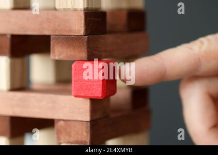 Wooden tower made of wooden brown cubes from which red cube is taken ...