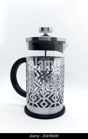 A glass French press of tea and a small glass of tea on a white table ...