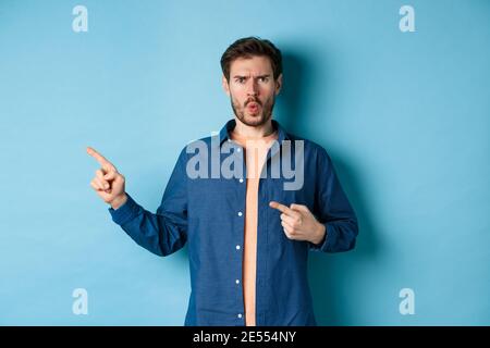 Shocked and offended young man frowning and looking hurt, pointing ...