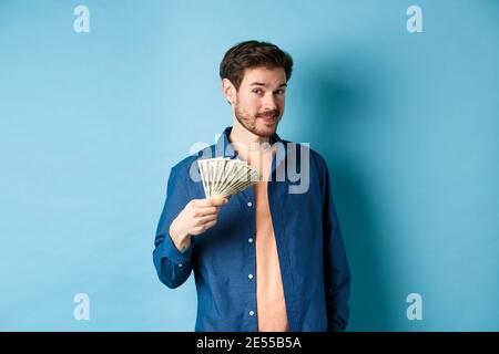 Unbothered rich guy showing cash and smiling, holding dollars in hand ...