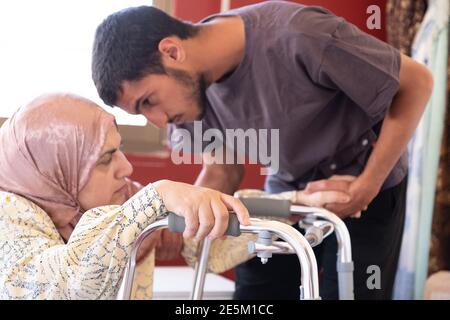 muslim woman with disability is trying to stand with her son's help ...