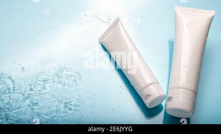 Cosmetic cream with water drops on green leaves on light background ...