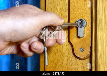 A hand puts the key in the keyhole. The key inserted in a wooden door ...