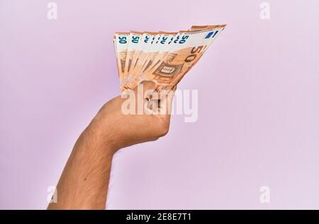 Hispanic hand holding 50 euro banknotes over isolated pink background ...