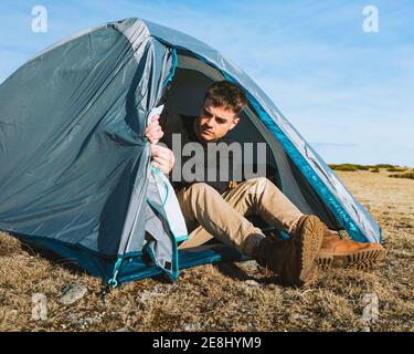 Full body of serious male traveler sitting on stone pillar near ...