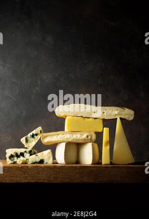 Wooden cutting board with cheese variety on dark concrete background ...