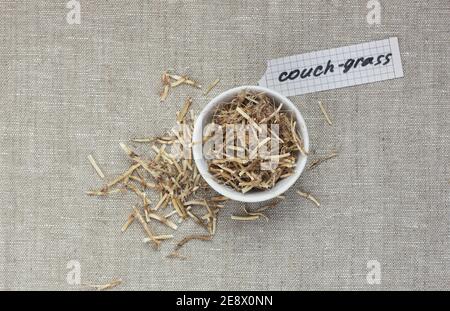 Couch-grass herbal roots in a bowl flat from above on linen textile ...