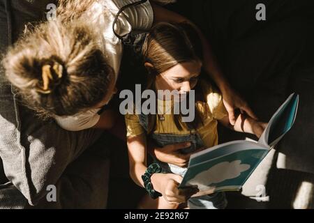 Two women mother and daughter reading book sitting on table at home ...