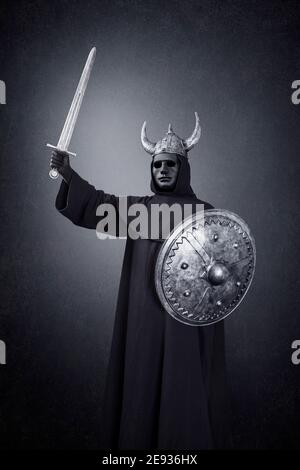 Scary figure with horned helmet, sword and round shield in the dark ...