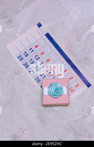 Calendar with date 14 FEBRUARY, gift and roses on table near light wall ...