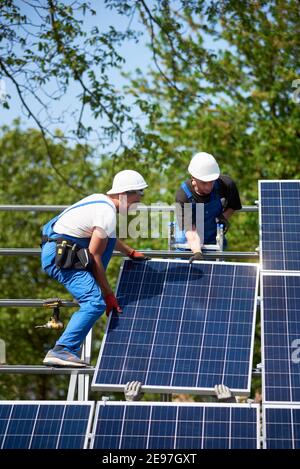 Team of technicians mounting heavy solar photo voltaic panel on tall ...
