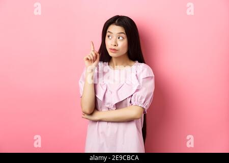 Beautiful asian girl raising finger and looking left at logo, having an ...