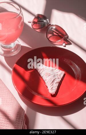 A nutella hand pie on a red plate . A glass and sunglasses on a pink ...