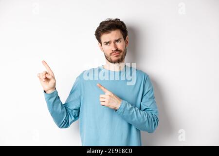 Skeptical and unimpressed young man grimacing, pointing fingers and ...