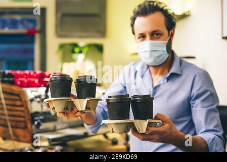 Handsome barista with a face mask making a cup of coffee at the coffee ...