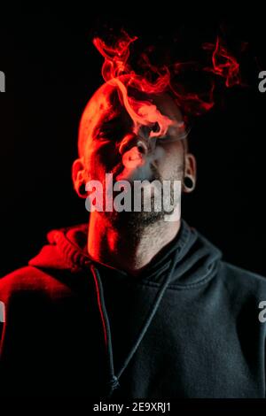 Serious male rocker smoking cigarette and looking at camera on black ...