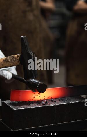 Unrecognizable craftsman hammering hot iron piece at anvil during ...